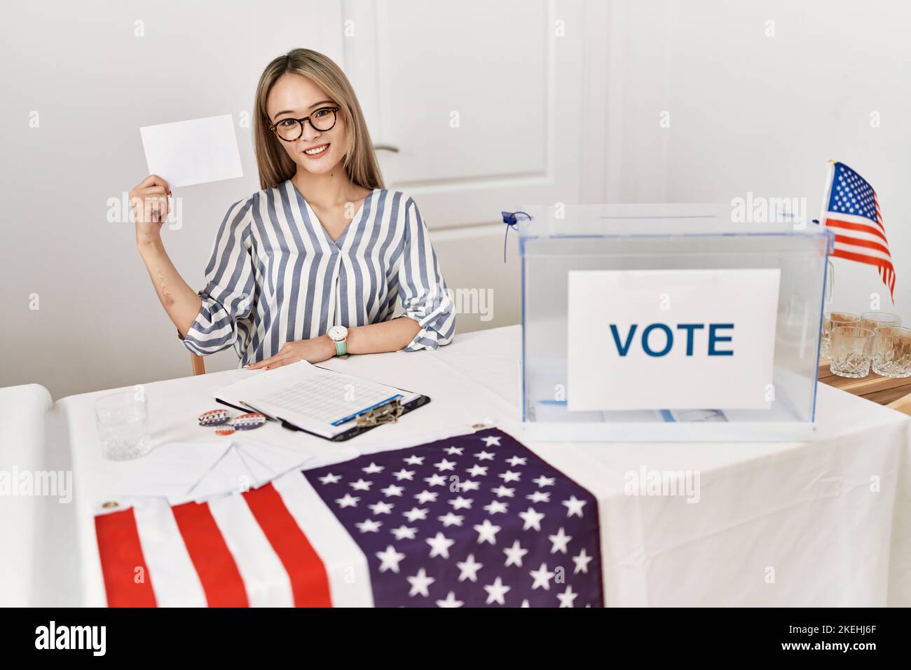 Young chinese woman sitting on election table holding vote at electoral ...