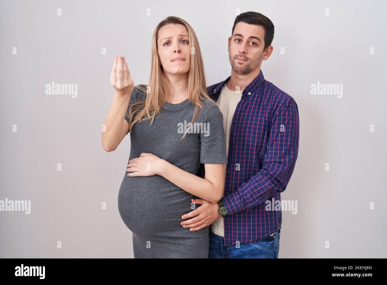 Young couple expecting a baby standing over white background doing ...