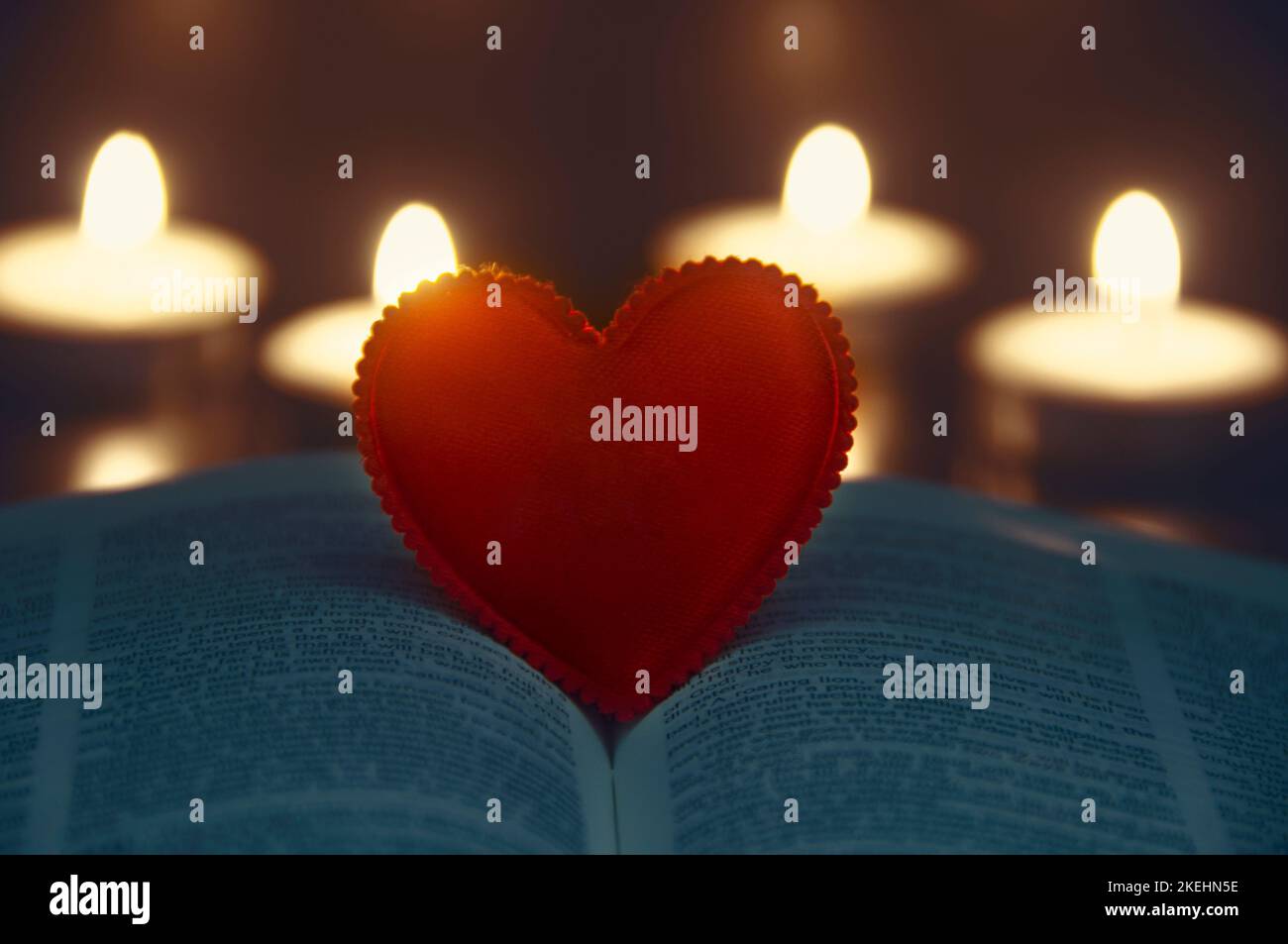 Red heart shape on Holy Bible with candle lights background ...