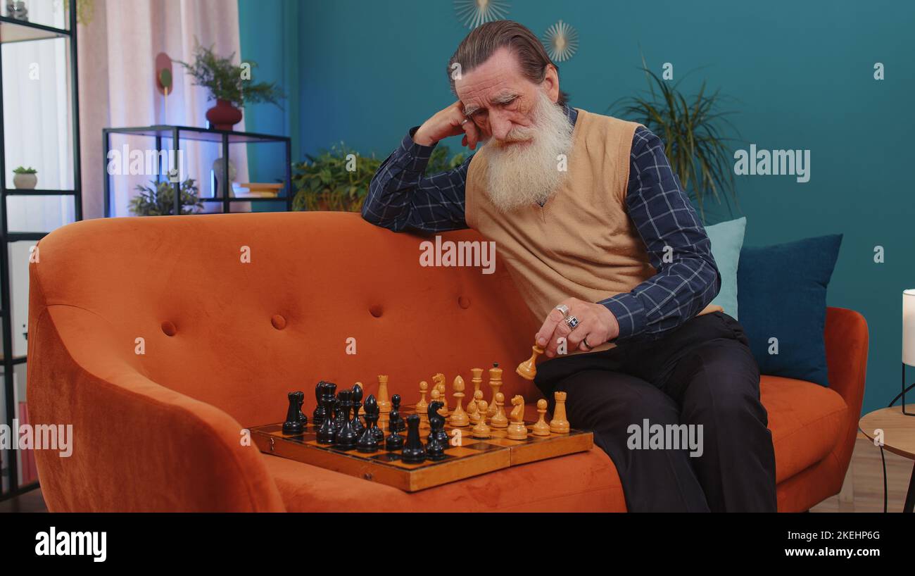 Focused senior grandfather man chessman sitting at home room couch ...