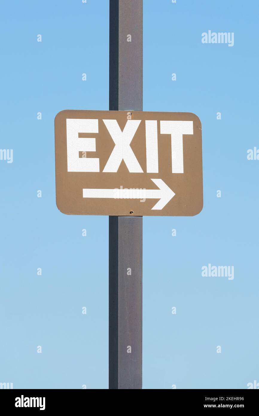 Brown exit sign attached to a post against blue sky background ...