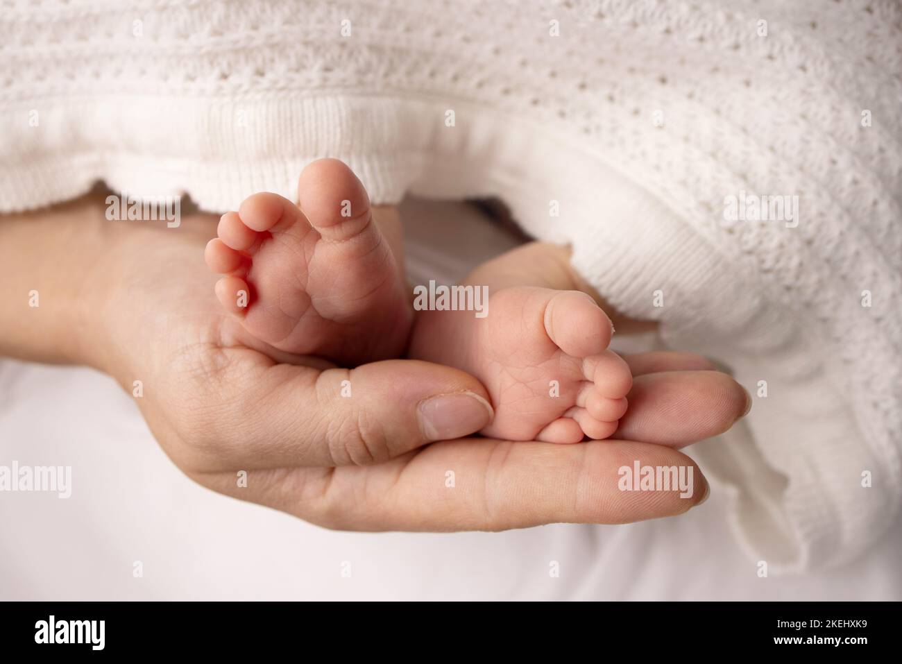 A mother hold the feet of a newborn child in a white blanket on white ...