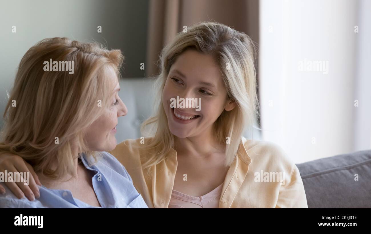Woman hugs her middle-aged mother talking seated on sofa Stock Photo ...