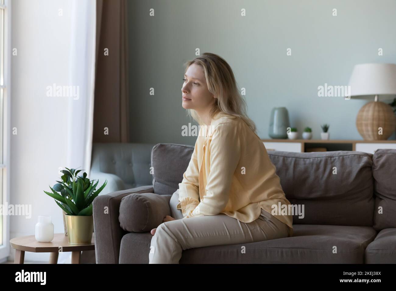 Pensive young woman resting on sofa looking out window Stock Photo - Alamy