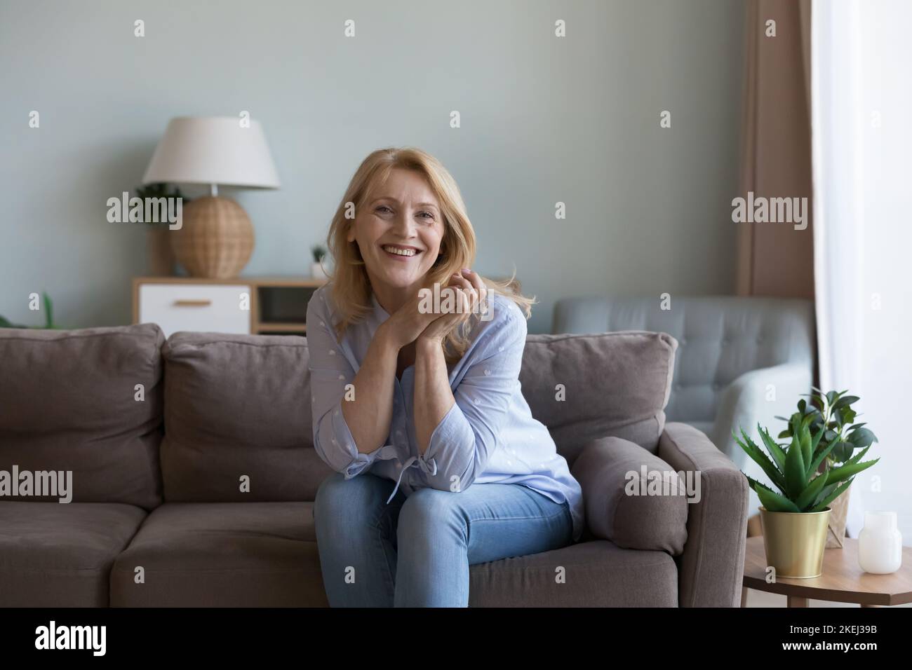 Pretty middle-aged woman posing for picture seated on sofa Stock Photo ...