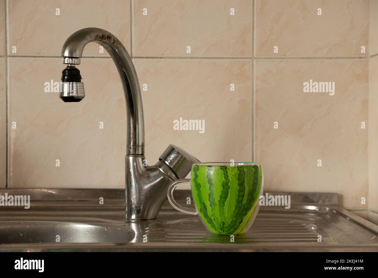 A cup with the image of a watermelon stands on a kitchen sink in ...