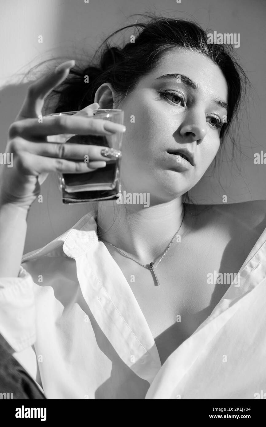 Young woman drinking alcohol from glass against sunny wall background ...