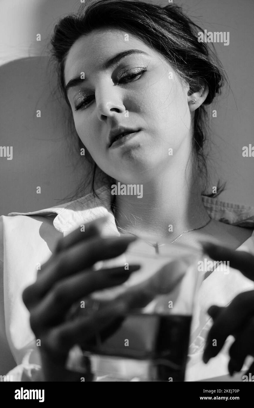 Young woman drinking alcohol from glass against sunny wall background ...