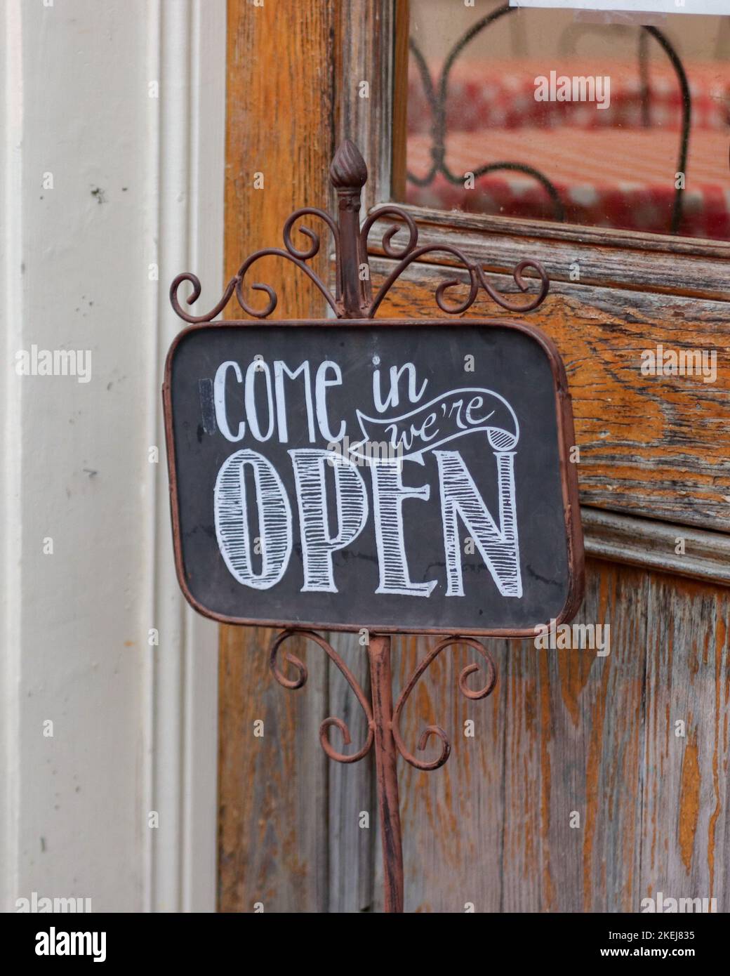 The vertical view of an open sign stands before an old wooden door ...