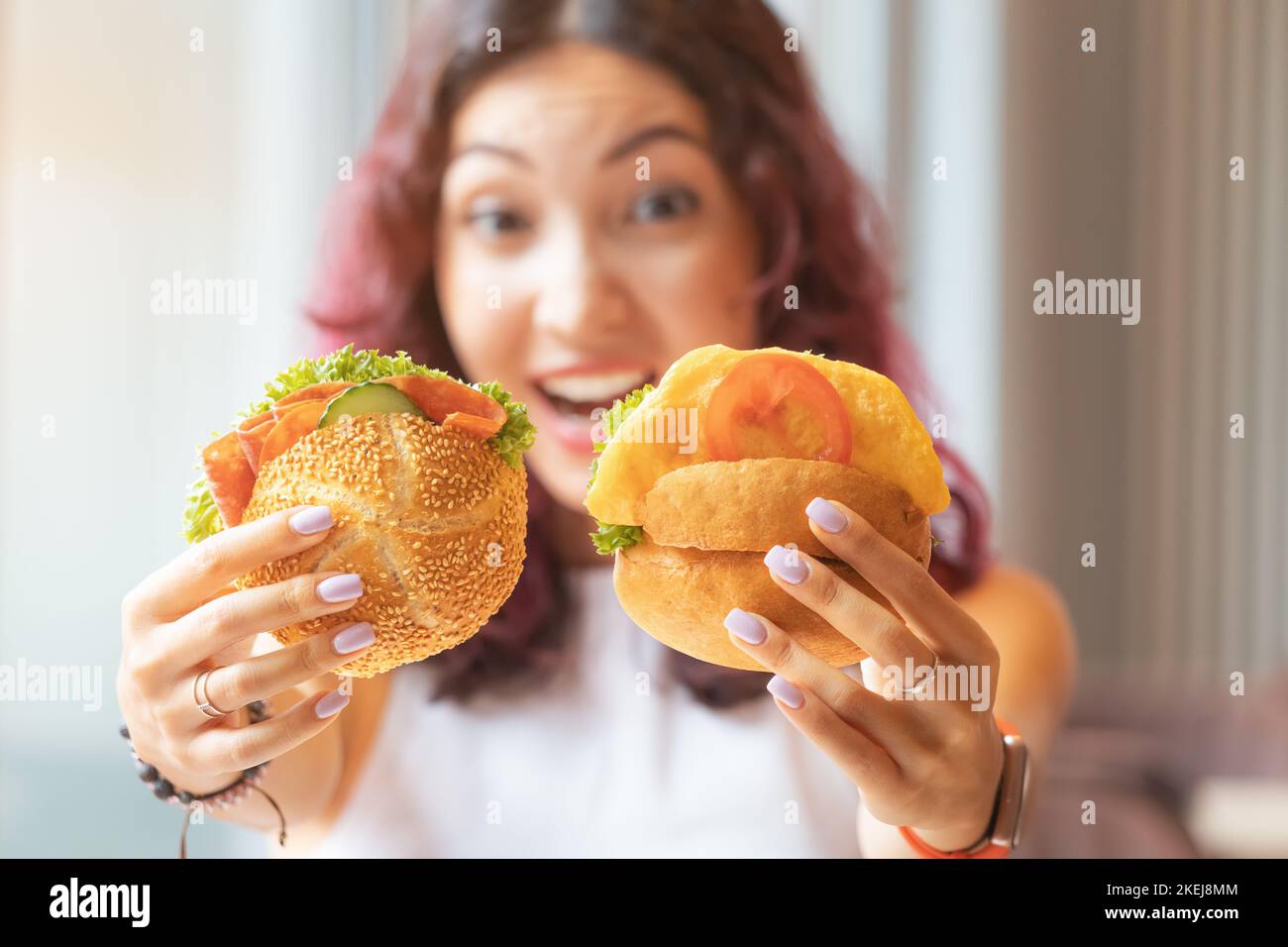 Happy asian girl eating two hamburger or sandwich with an appetite in a ...