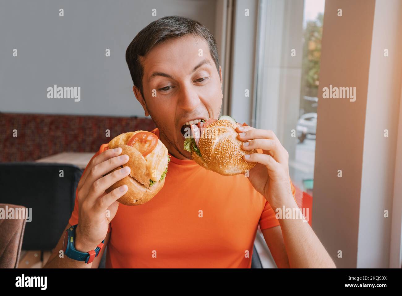 Happy man eating two hamburger or sandwich with an appetite in a fast ...