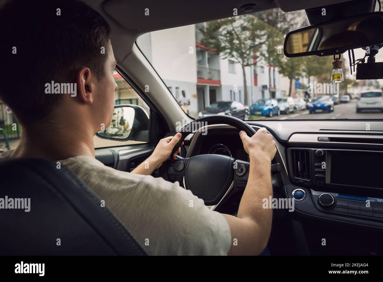 Confident young man driving car on the city streets. Teen driver keeps ...