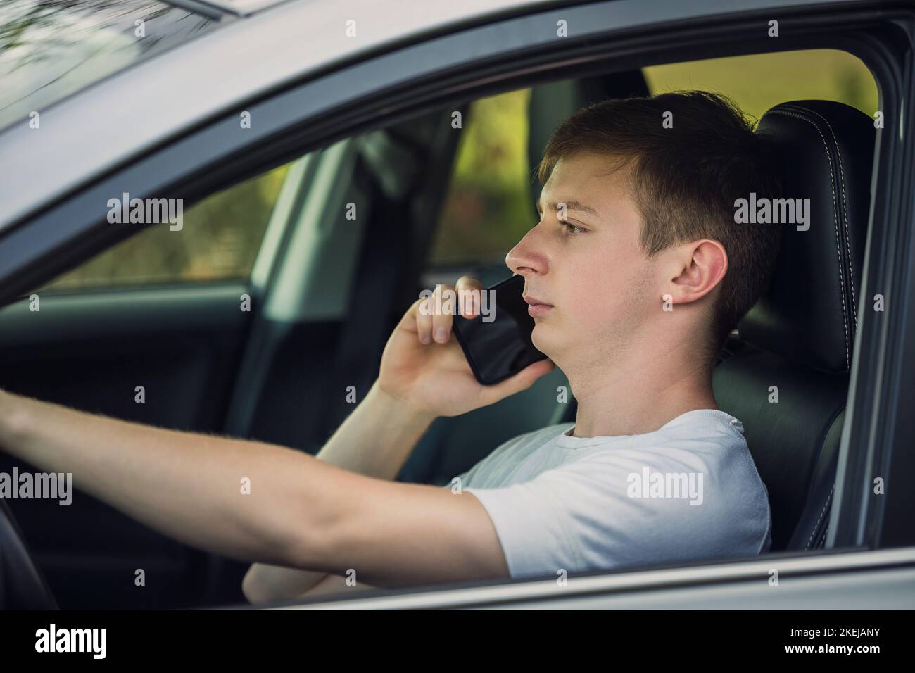 Young man unsafe driving while phone talking in front of the steering ...