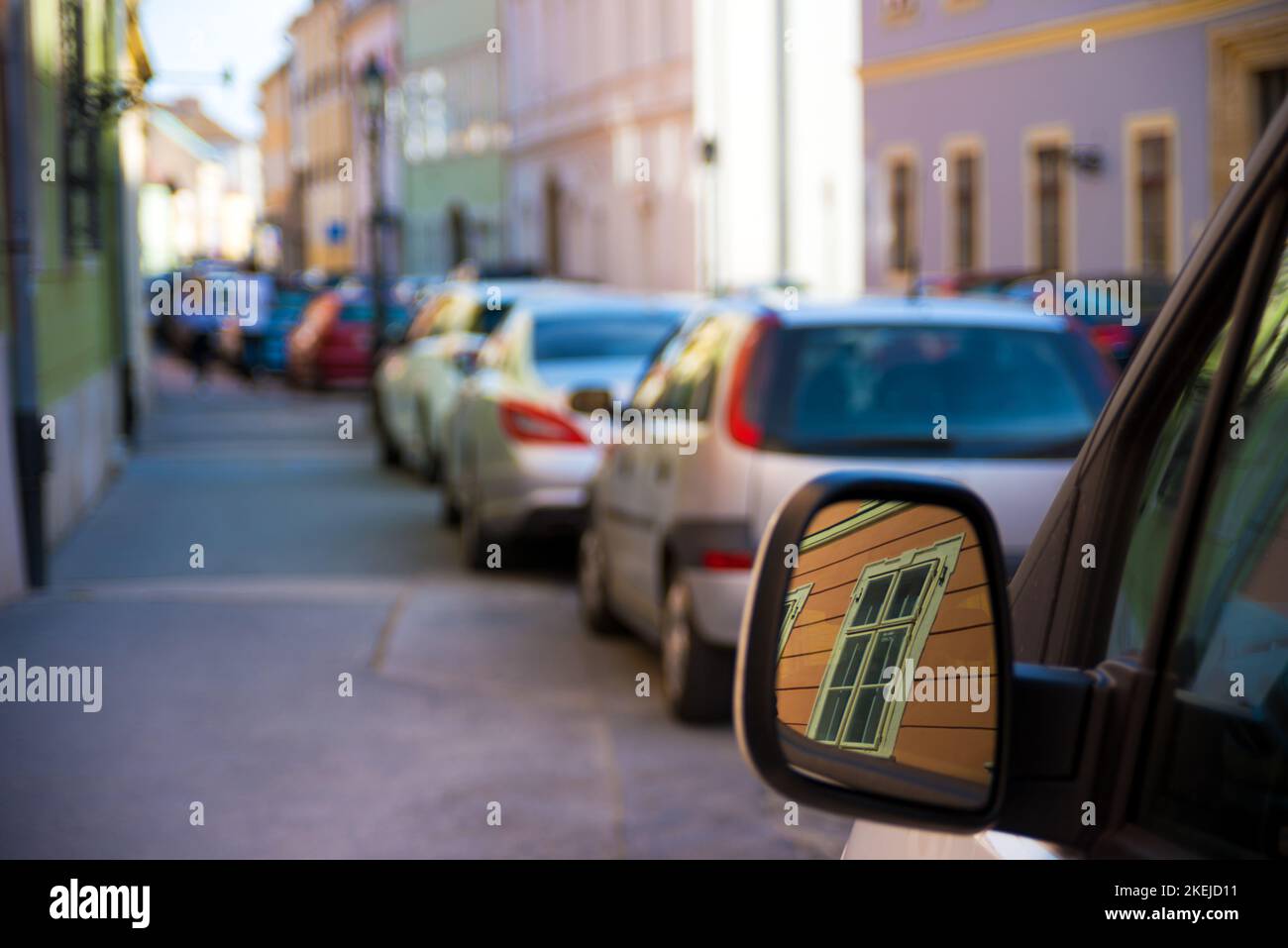 Cars parked on old city street. Window reflection in rear view mirror ...