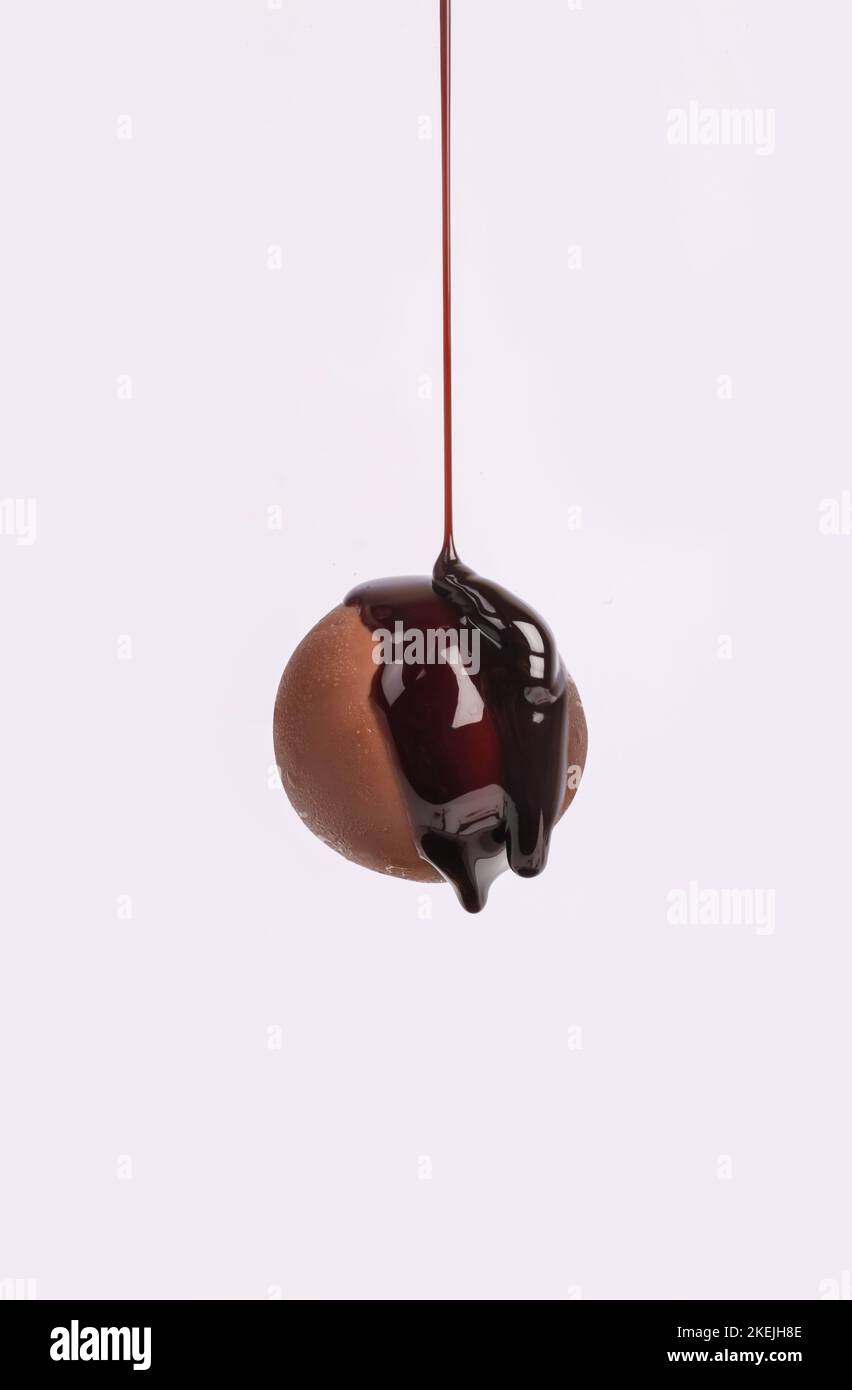 A vertical closeup of syrup dipping on a chocolate ball on a white ...