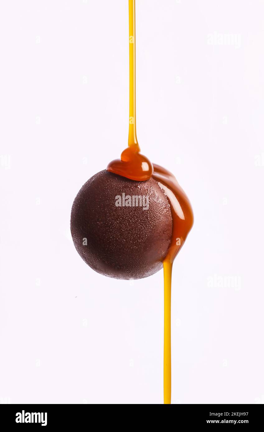 A vertical closeup of honey dipping on a chocolate ball on a white ...