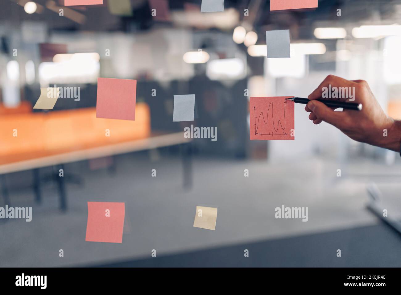 Businessman hand's is writing on sticky notes on board in modern office ...