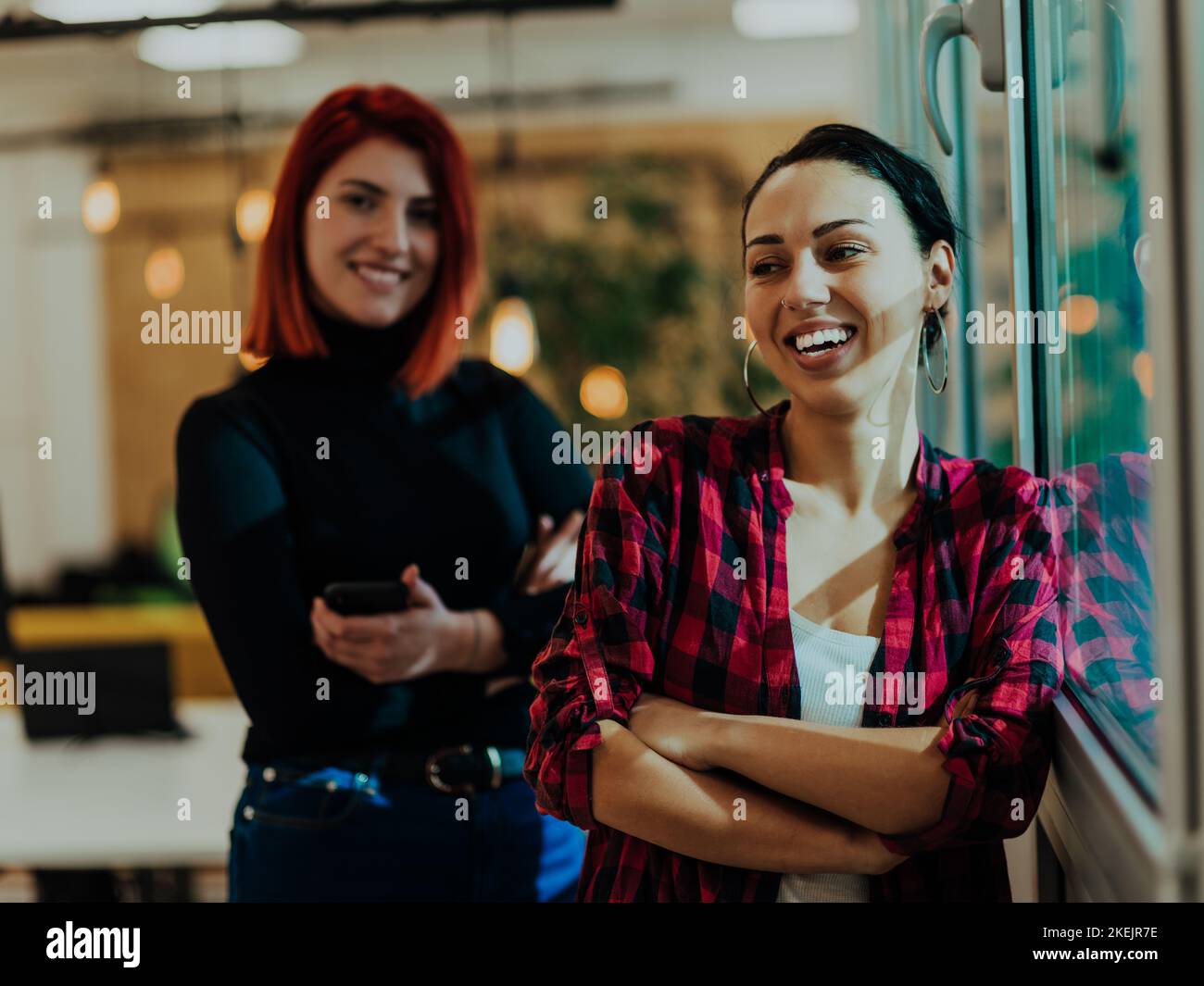 Portrait of two modern young women by the window in the night office ...