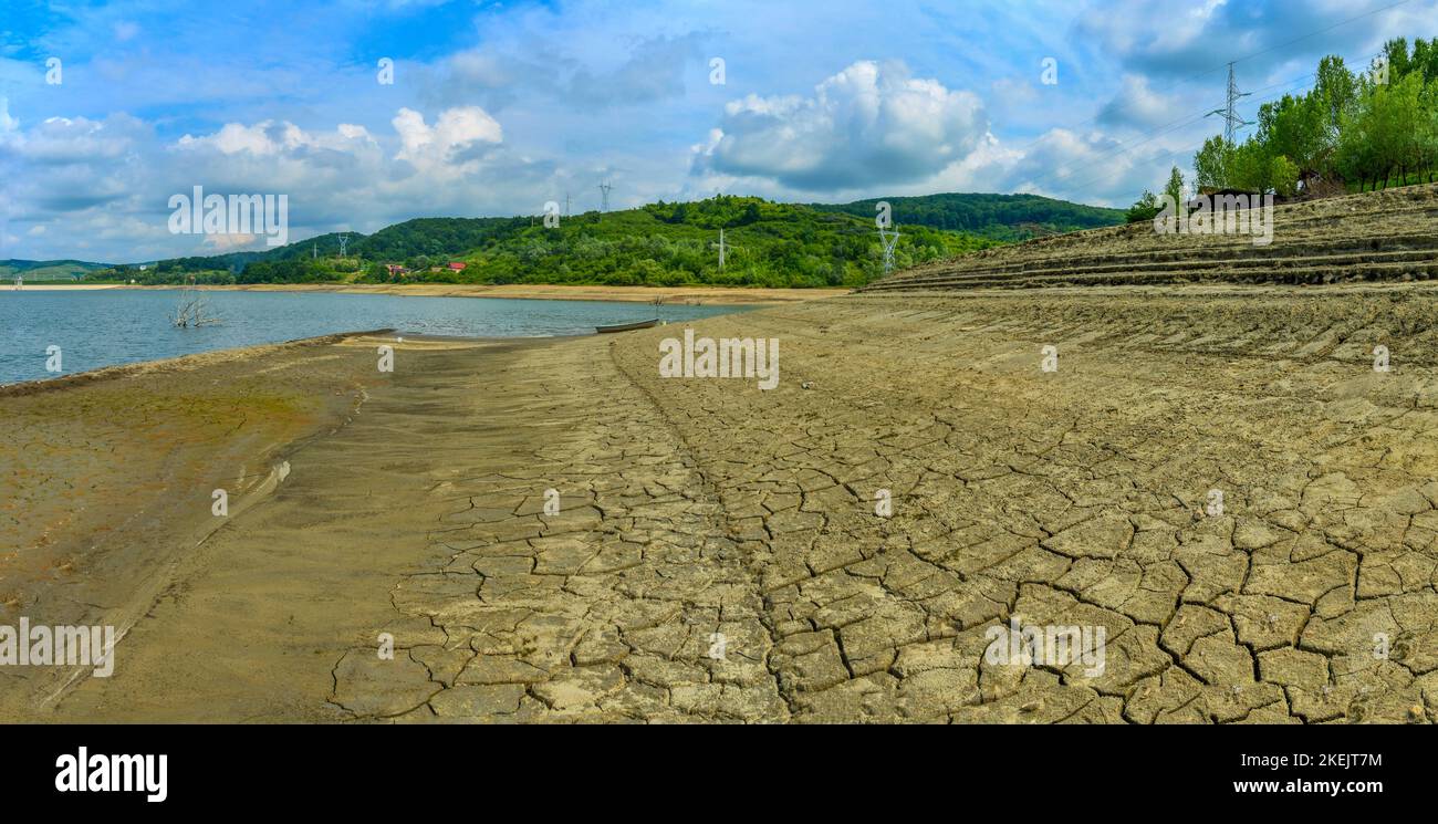A landscape of a lake with dry and cracked shore and low water due to ...