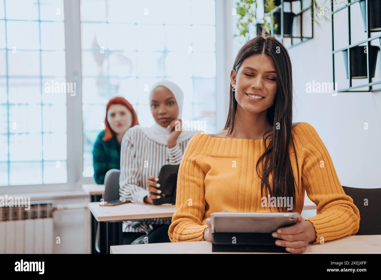 A group of diverse young men and women sit in a modern classroom and ...