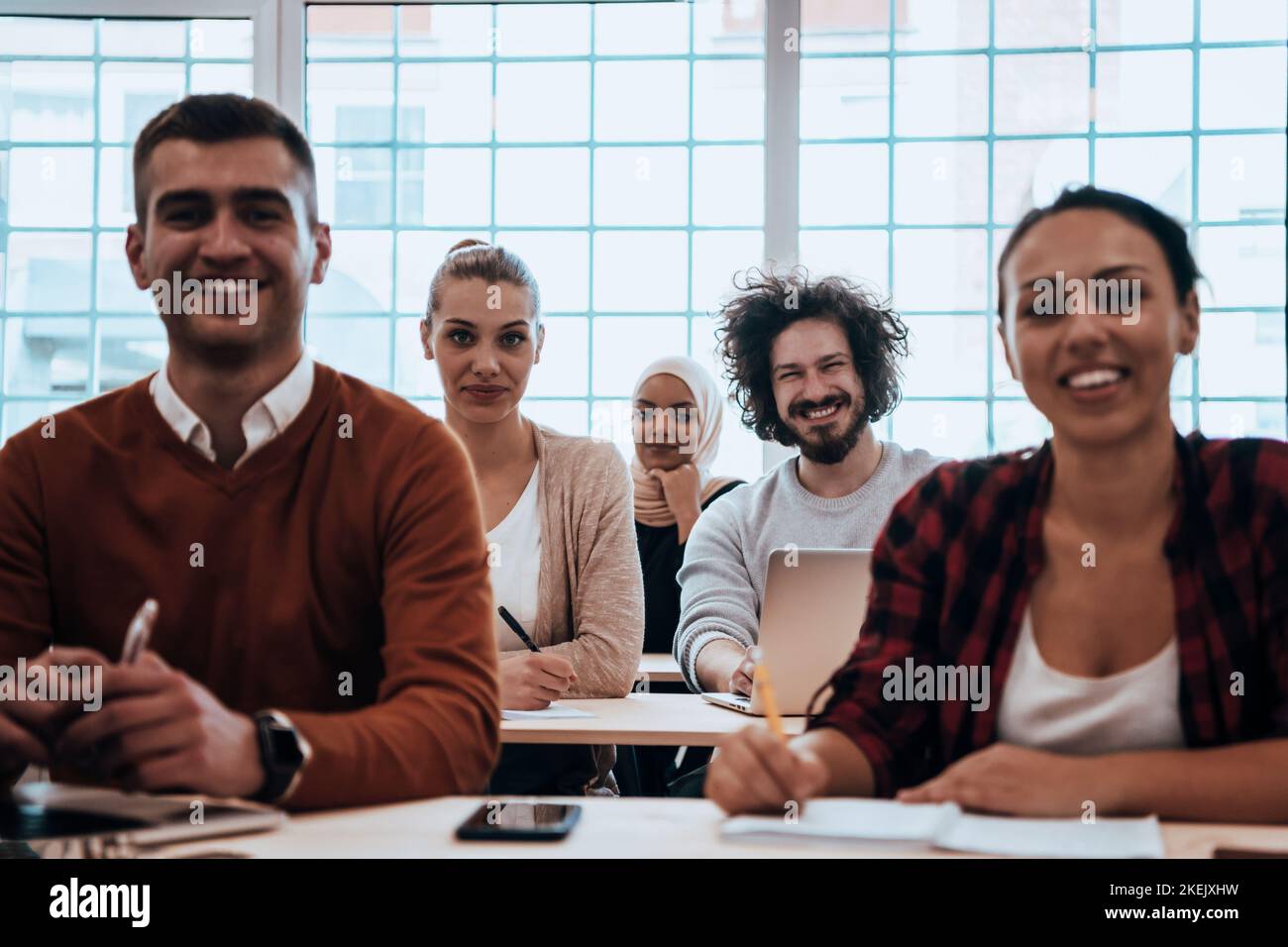 A group of diverse young men and women sit in a modern classroom and ...