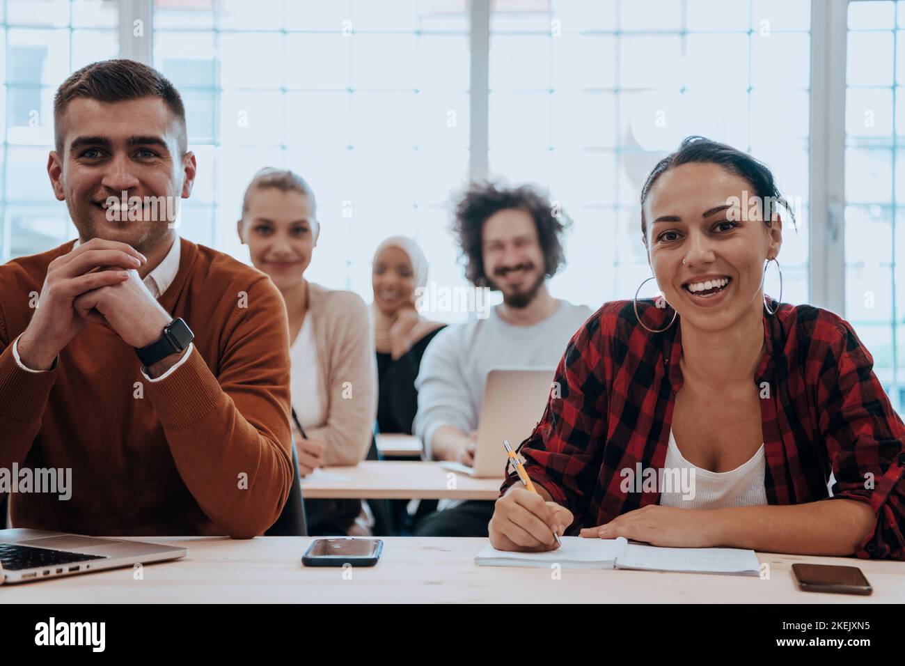 A group of diverse young men and women sit in a modern classroom and ...