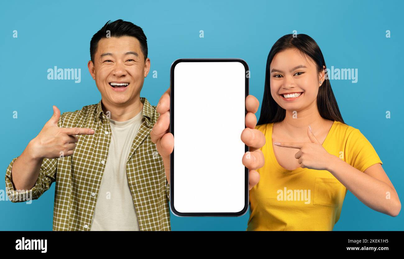 Smiling millennial asian couple show finger on big smartphone with ...