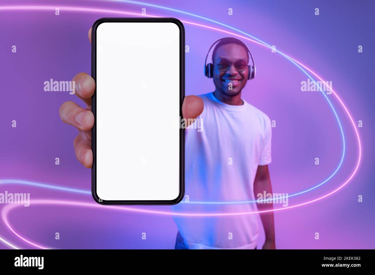 Cheerful black guy showing cell phone, using wireless headphones ...
