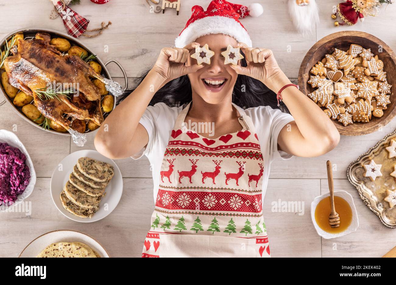 A cheerful cook in a Christmas apron lies on the ground and covers her ...