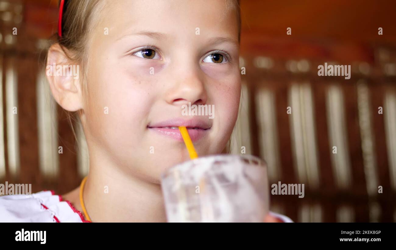 happy smiling teen girl child drinks a milkshake in cafe. she is dressed in Ukrainian national ...
