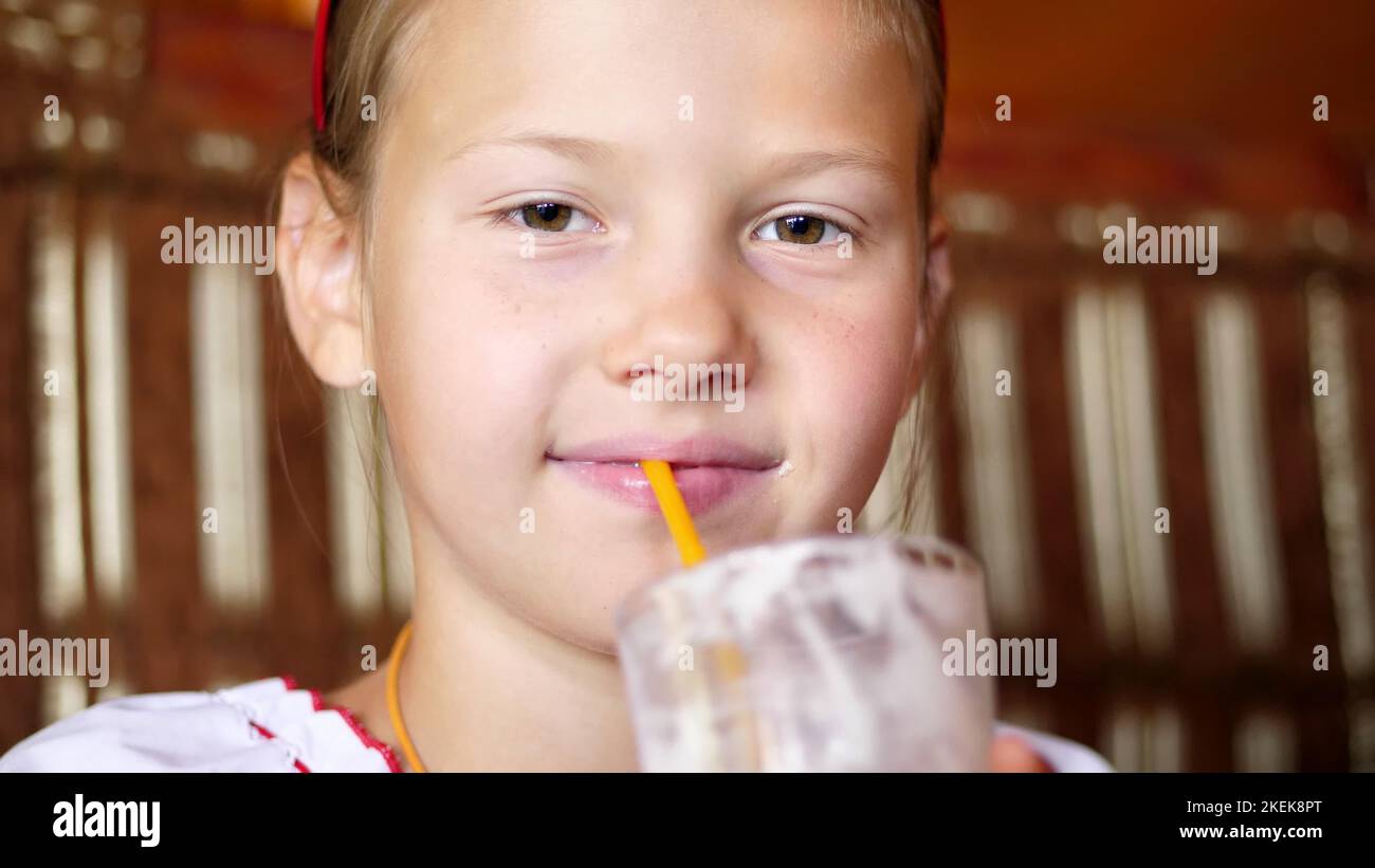 happy smiling teen girl child drinks a milkshake in cafe. she is dressed in Ukrainian national ...