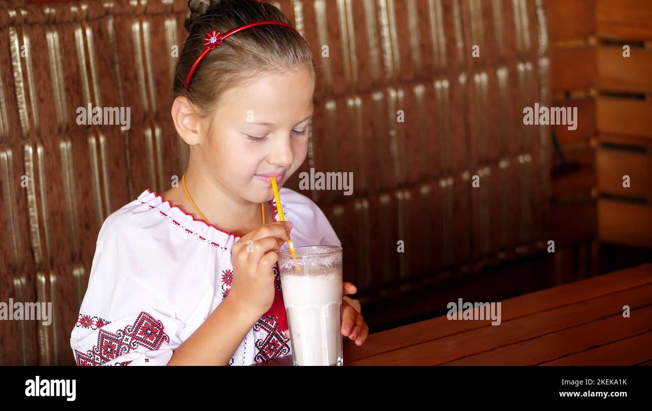 happy smiling teen girl child drinks a milkshake in cafe. she is ...