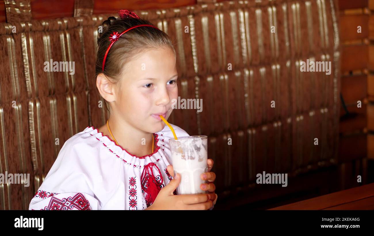 happy smiling teen girl child drinks a milkshake in cafe. she is ...