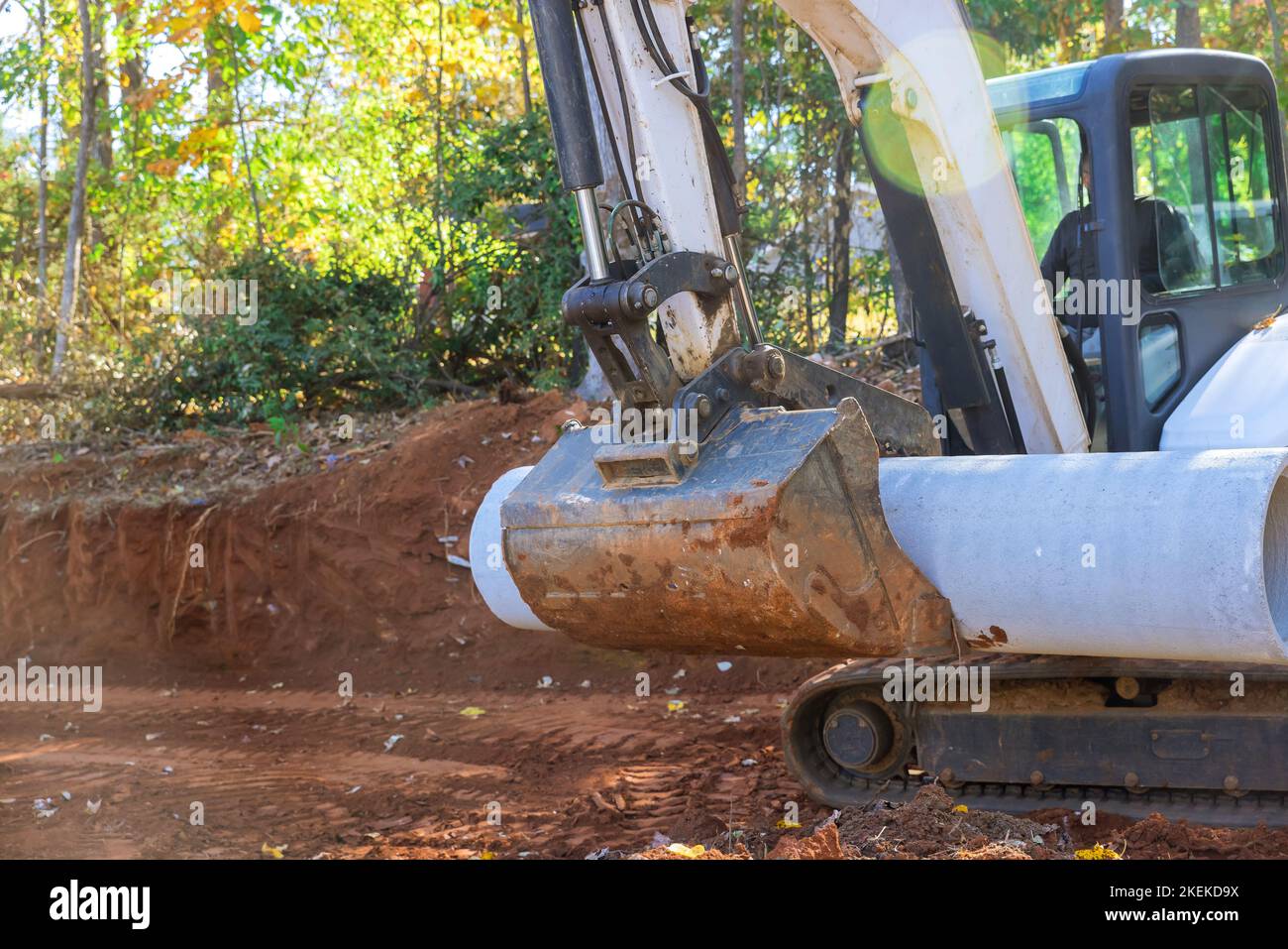 Worker who use tractor to lift concrete sewage pipes in ground are ...