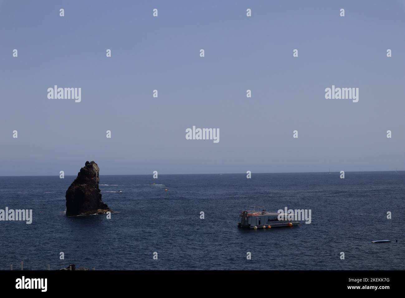 A sea stack and a bunker barge in the blue water against the clear sky ...