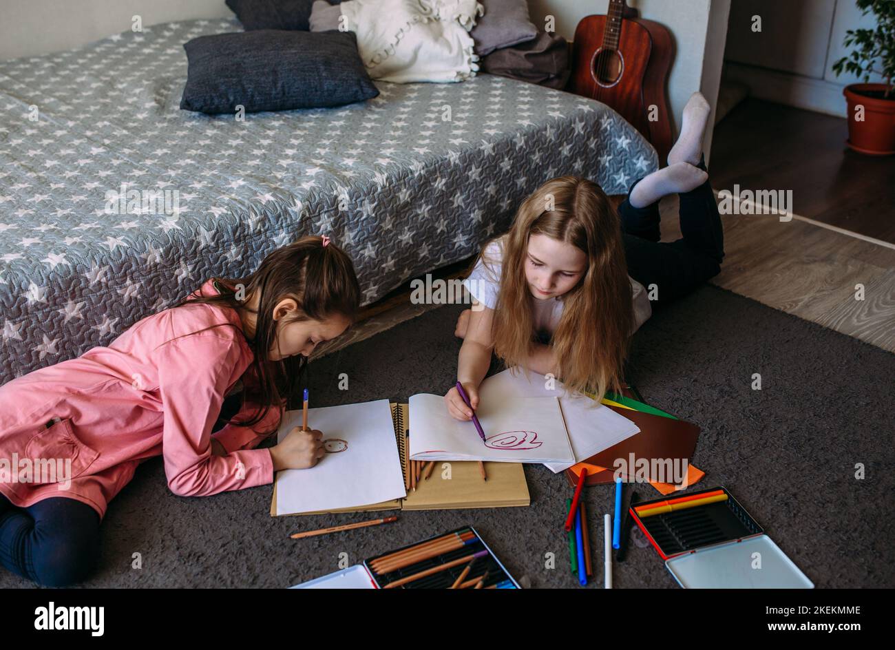 Two girls friends play at home, draw with pencils and felt-tip pens and ...