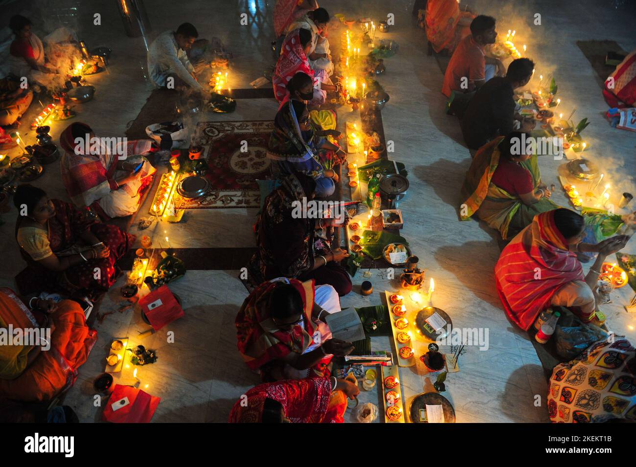 Hindu devotees sit together with lamps on the floor at Loknath Temple ...