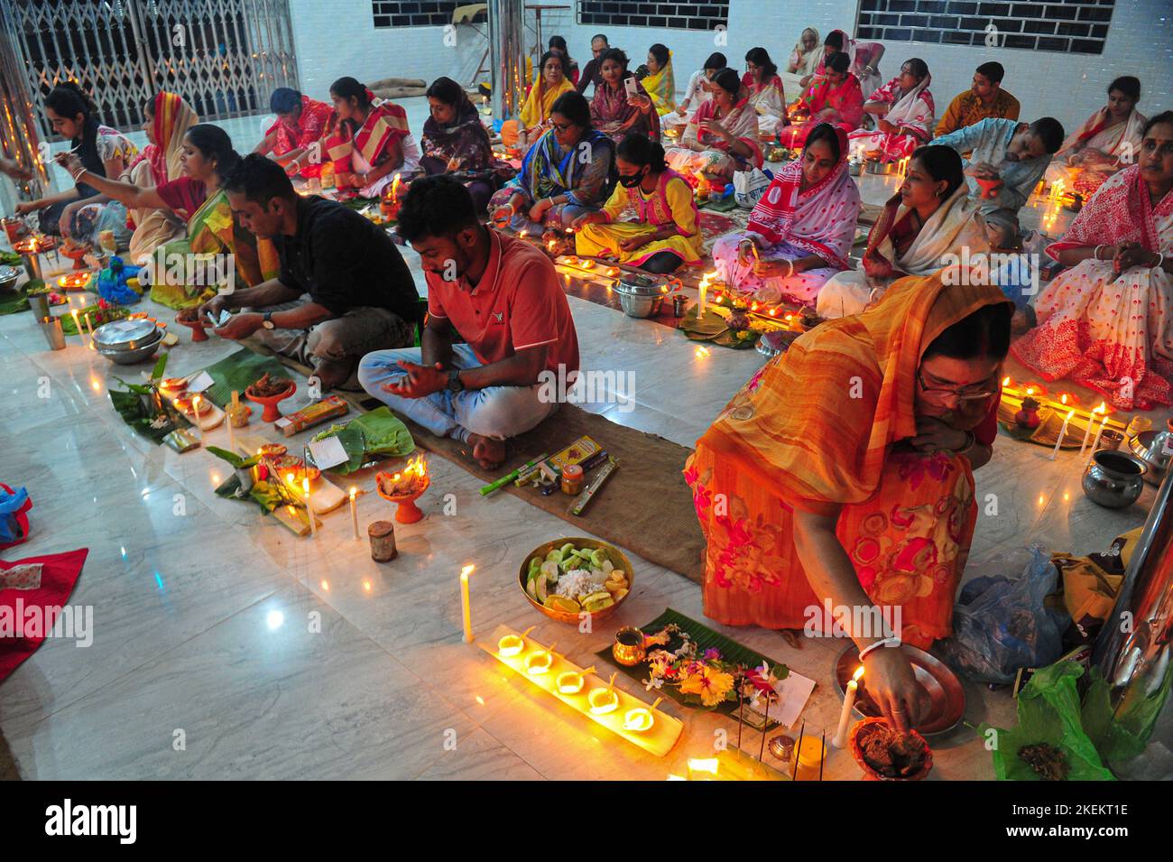 Hindu devotees sit together with lamps on the floor at Loknath Temple ...