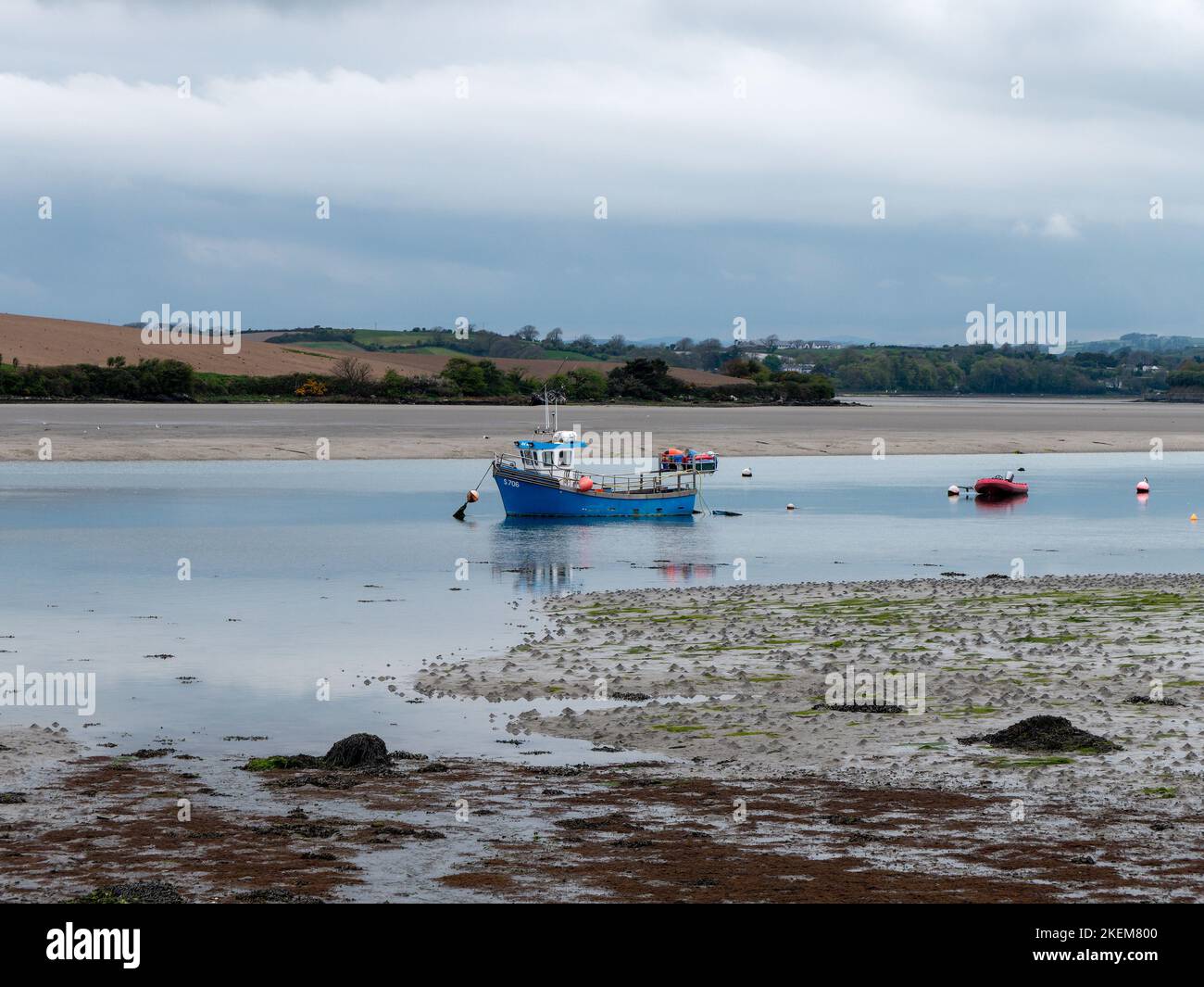 Clonakilty Bay at low tide. A small blue fishing boat is anchored. Open ...