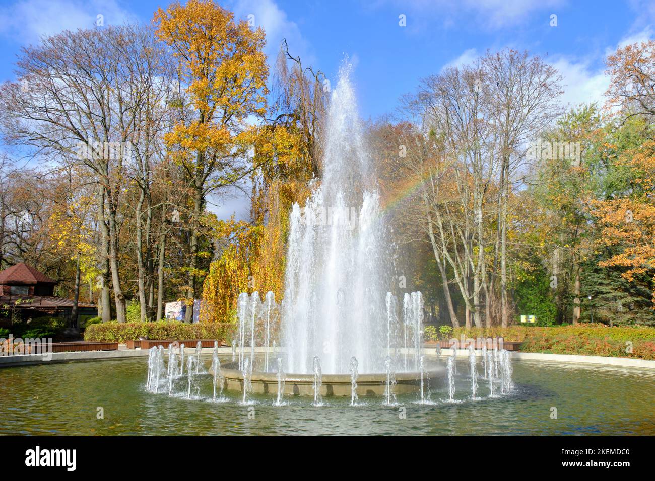 Beautiful fountain with blue sky and trees with yellowed autumn foliage ...