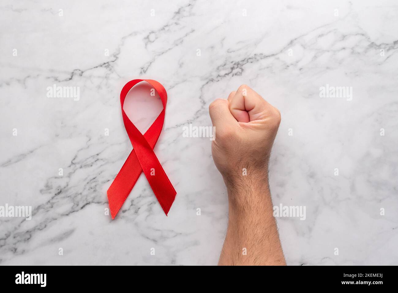 A clenched fist on a marble table next to a red ribbon symbolizing ...