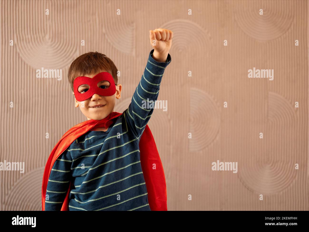 Brave cheerful boy in superhero cape and mask standing with hand on ...