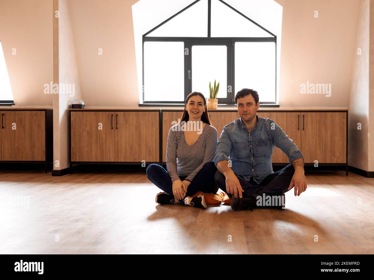 Happy couple sitting on a wooden floor in an apartment. They are happy ...