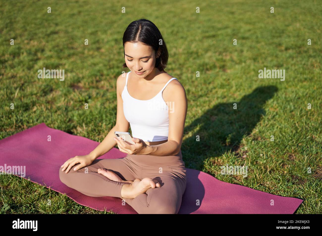 Asian girl follows yoga training app, looking at smartphone, meditating ...