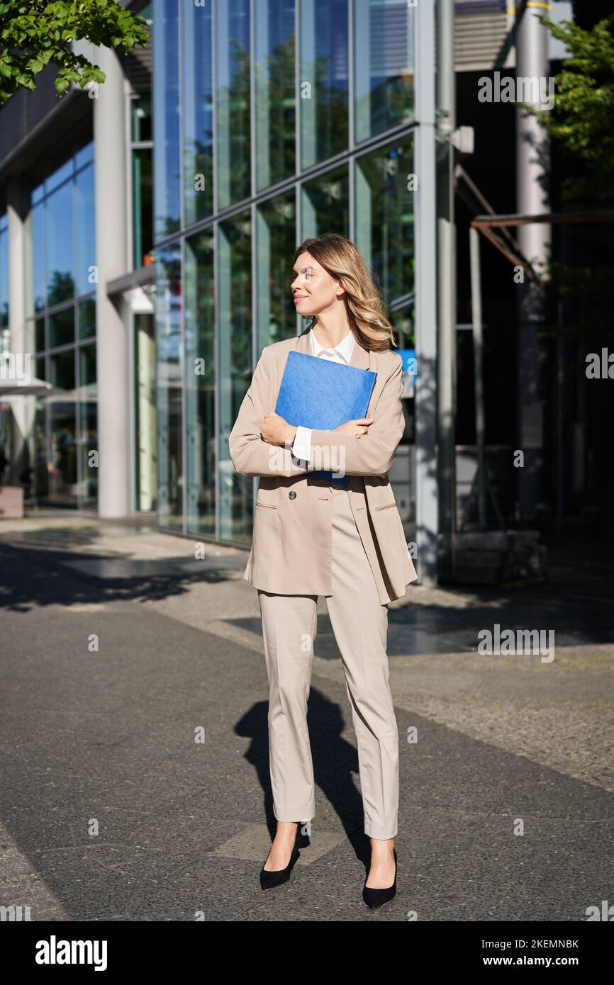 Vertical shot of businesswoman with folder, standing on a street near ...