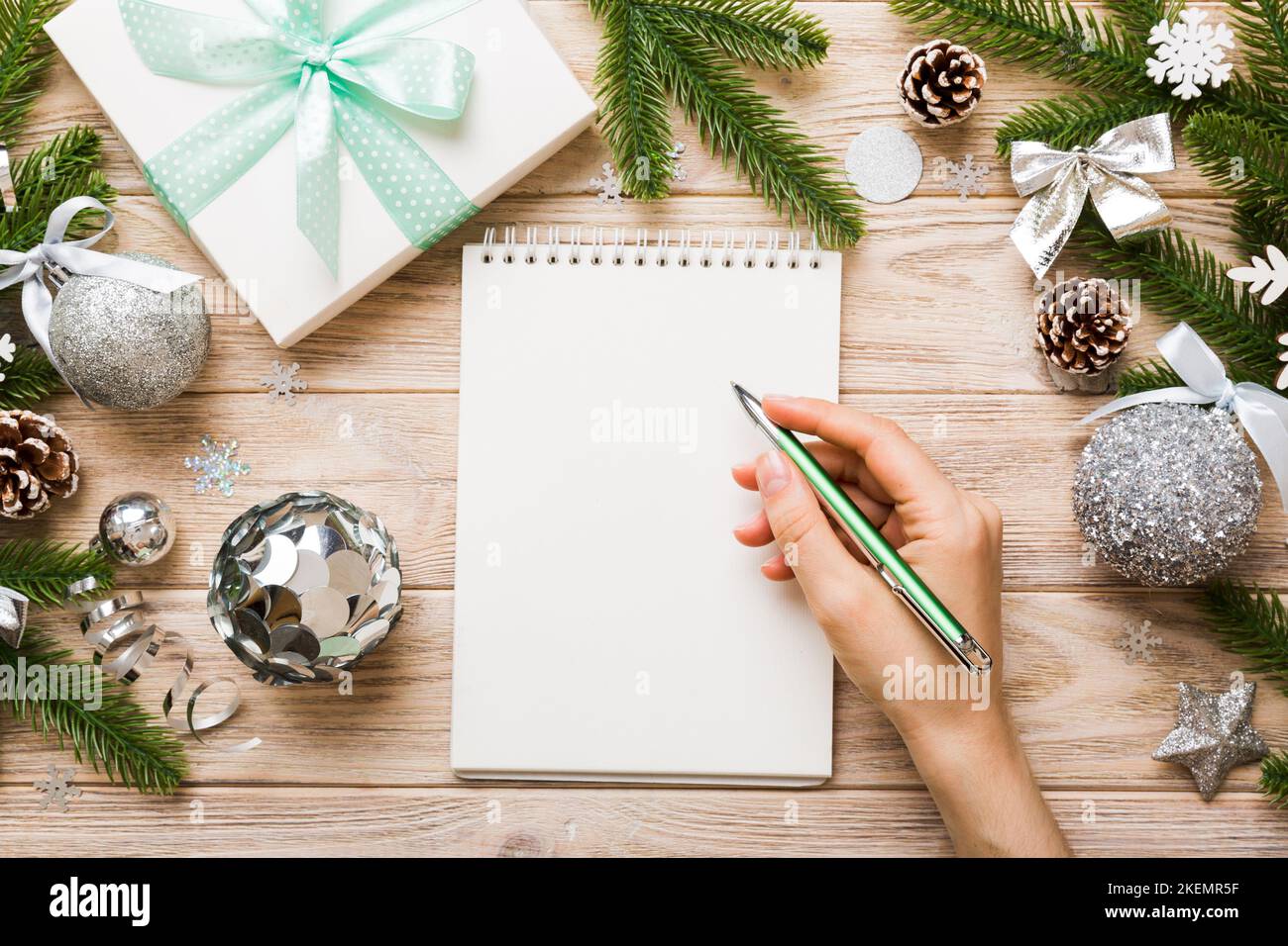 Woman writing Christmas to do list on notebook on colored background ...