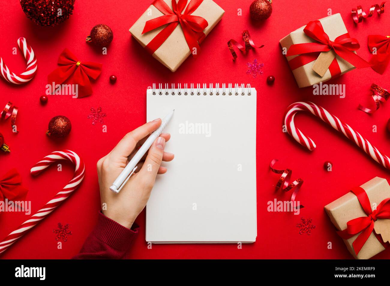 Woman writing Christmas to do list on notebook on colored background ...