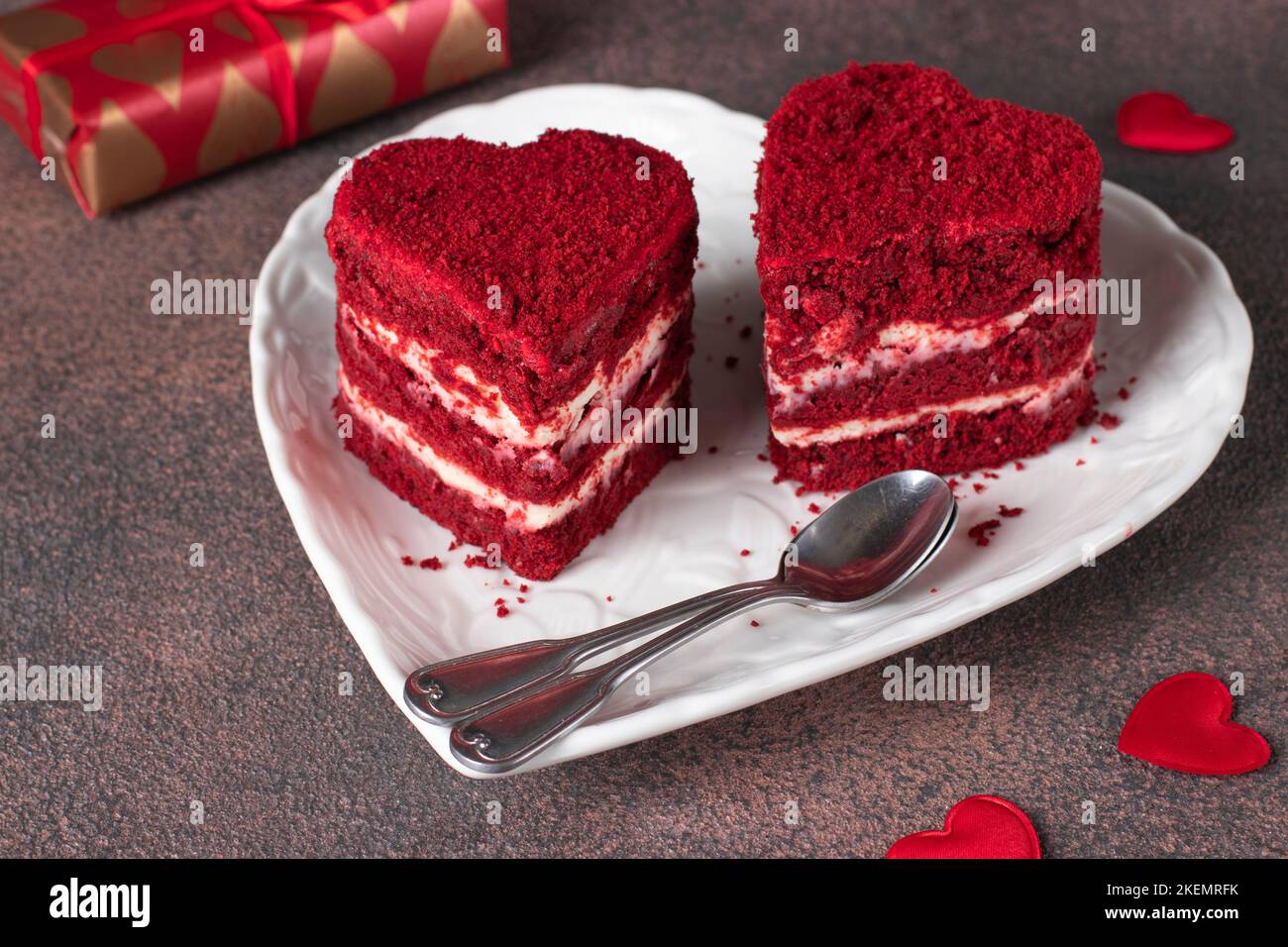 Two cakes Red velvet in the shape of hearts on white plate and gifts on ...