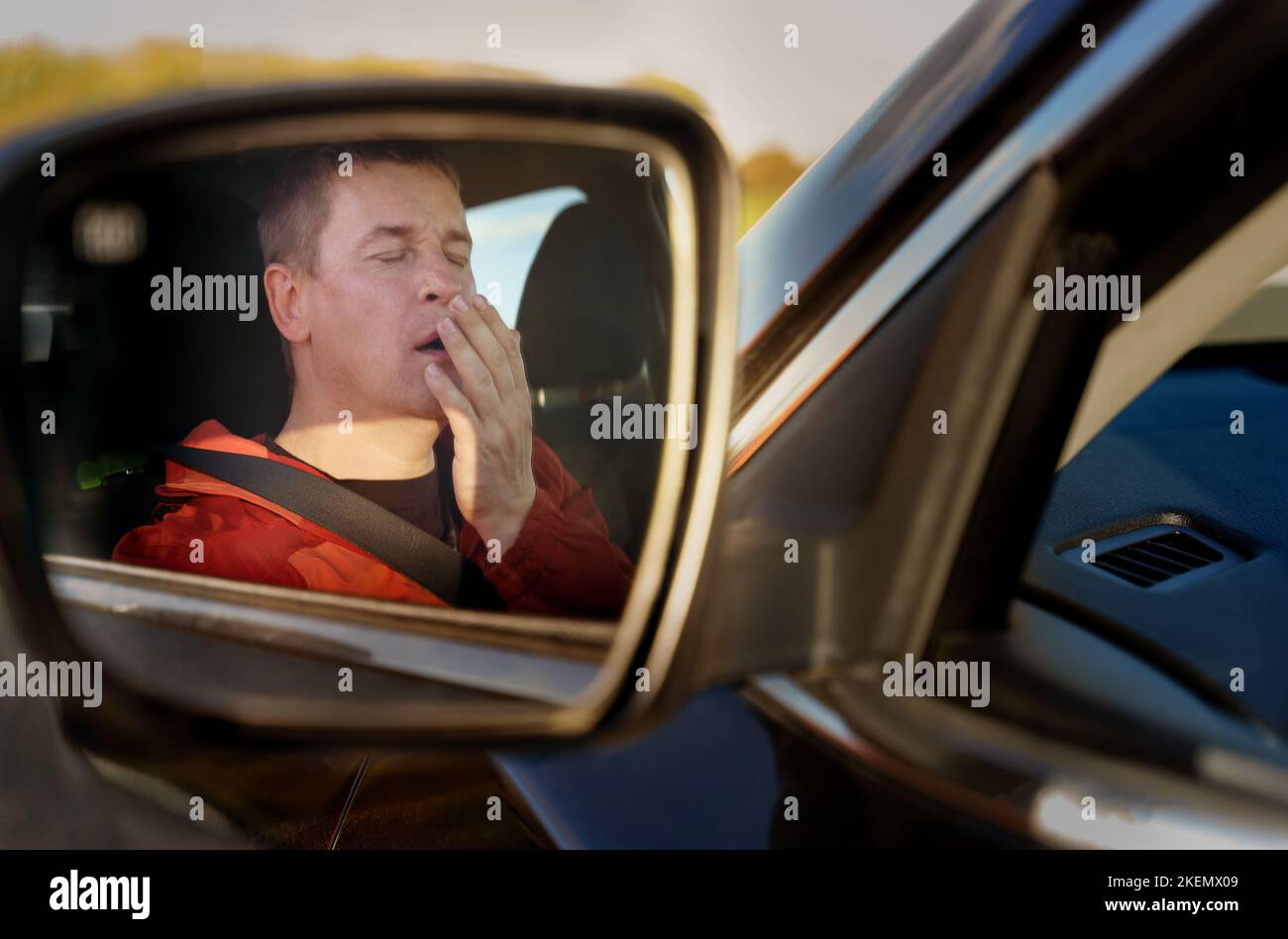 A tired driver yawns while covering his mouth with his hand while ...
