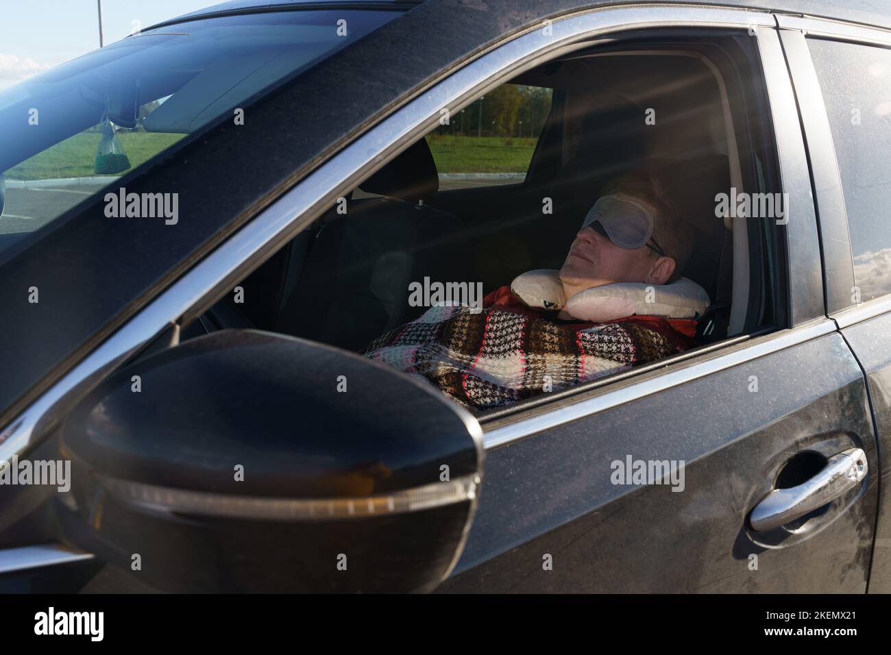 A tired driver sleeps in the car during the day, covered with a blanket ...